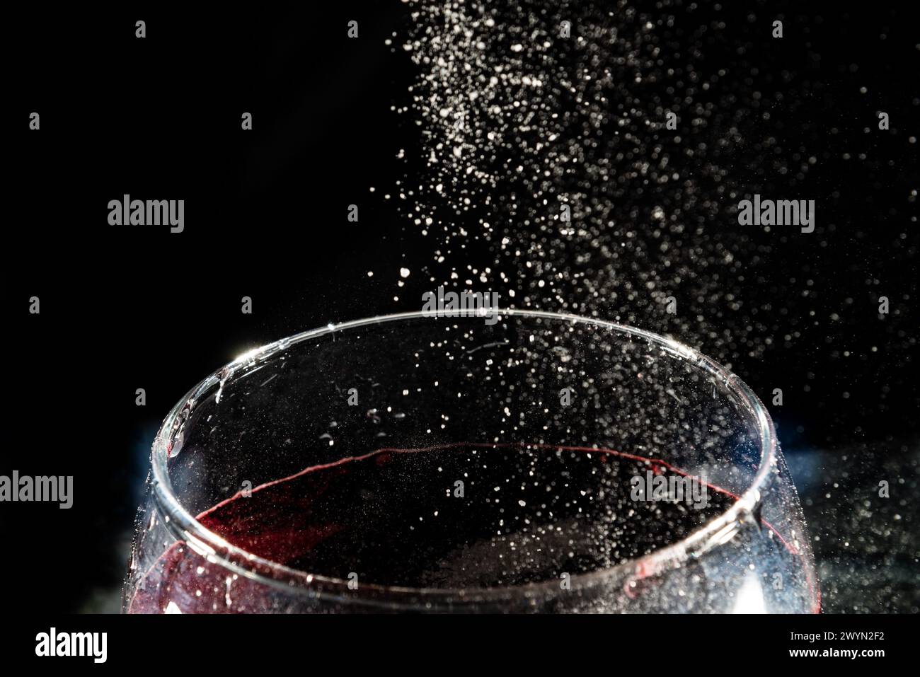 White powder falling into a transparent glass cup filled with wine ...