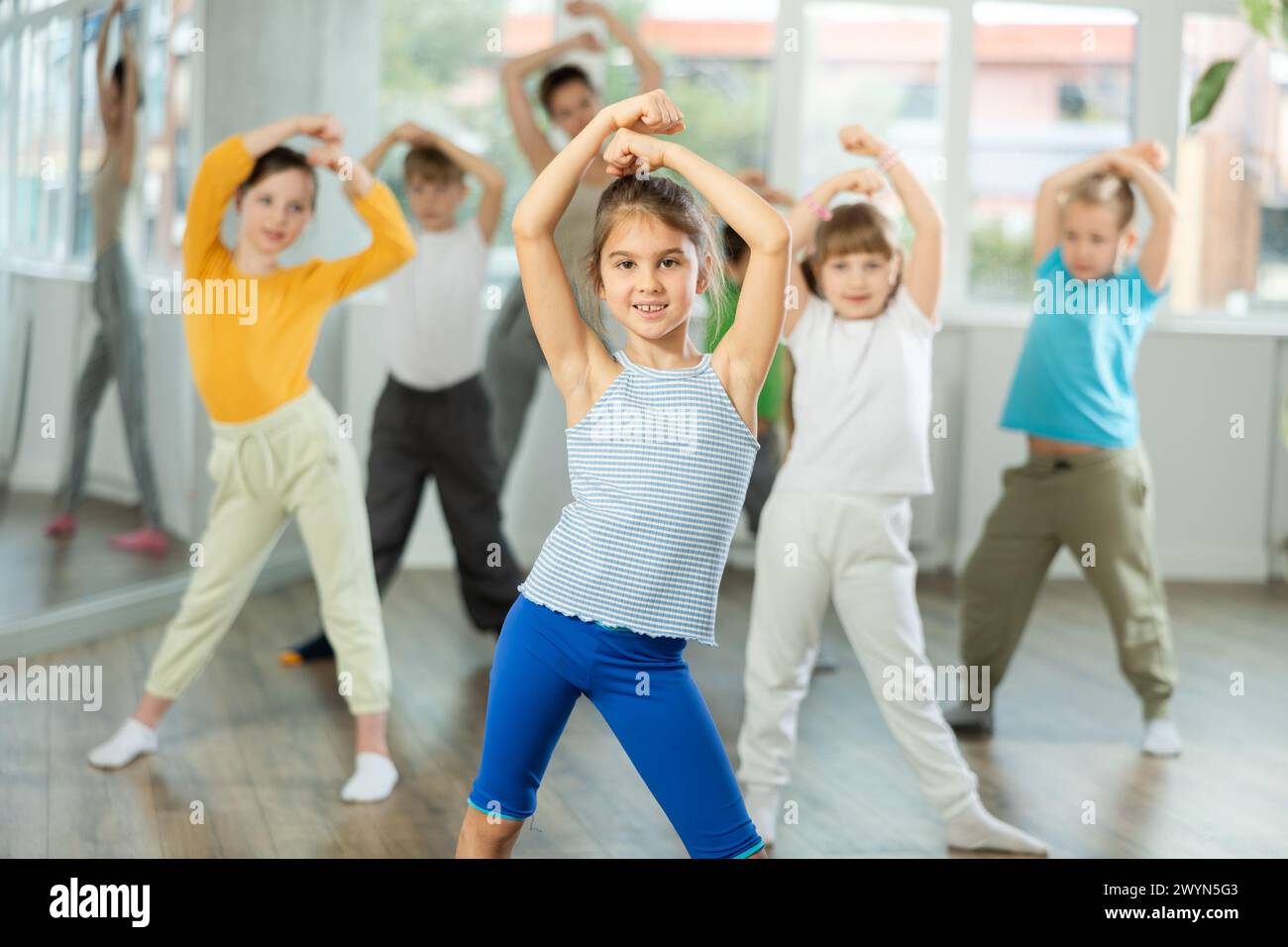 Positive juvenile girl engaged in breakdancing in training room with ...