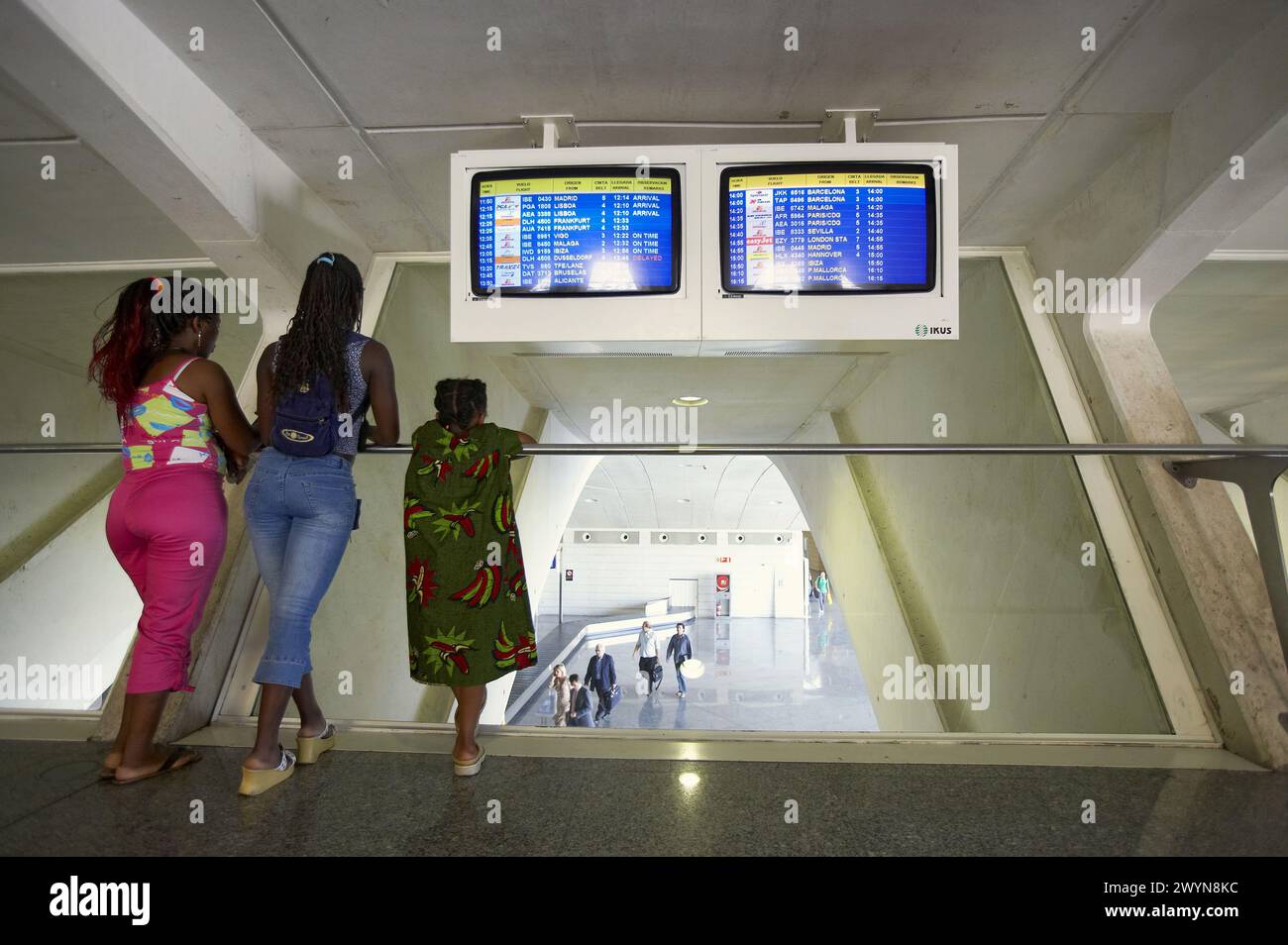People waiting by flight information boards in the Bilbao airport by ...