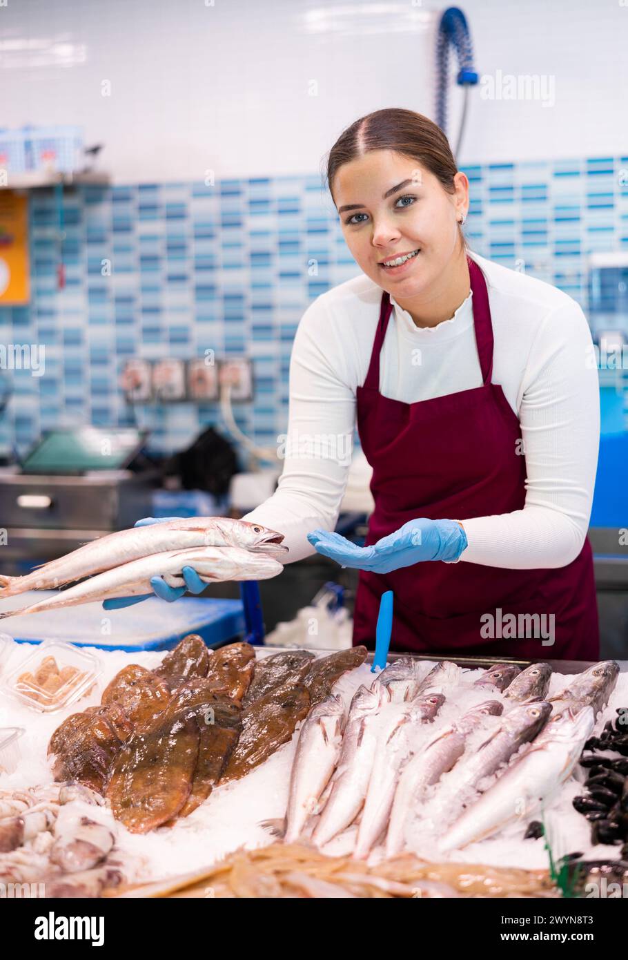 Female seller standing near counter offering fresh fish striped red ...