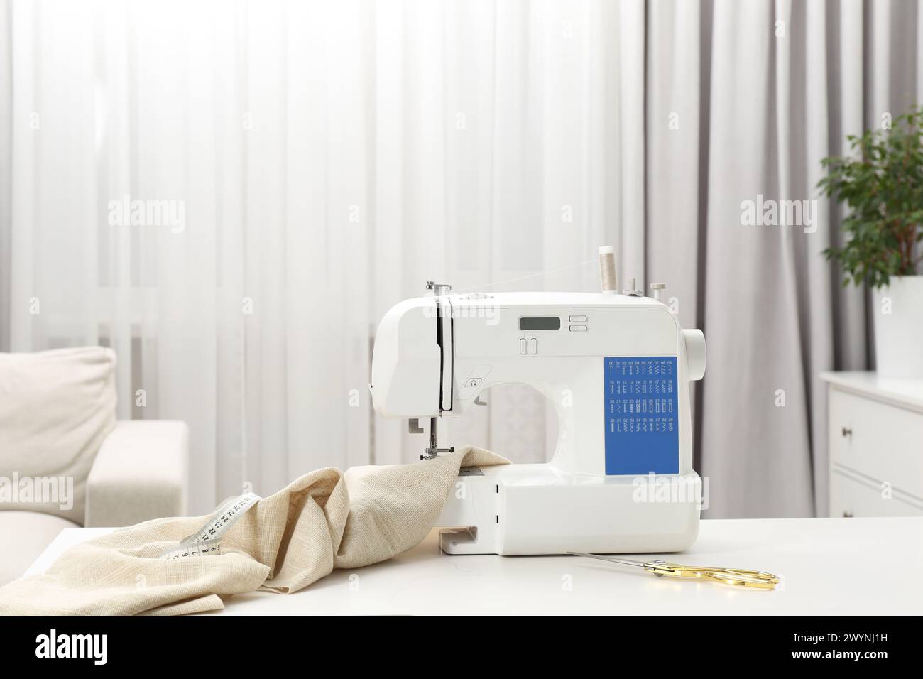 Sewing machine, measuring tape, scissors and fabric on white table in ...