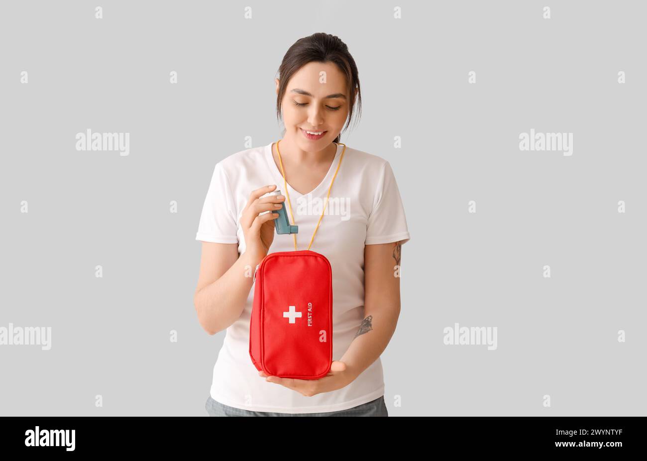 Sporty young woman with inhaler and first aid kit on light background ...