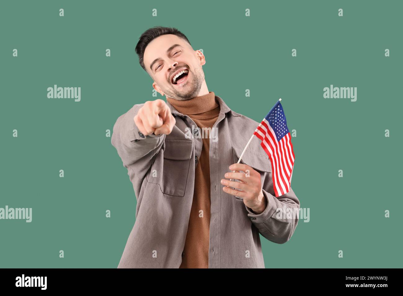 Laughing young man with USA flag pointing at viewer on green background ...