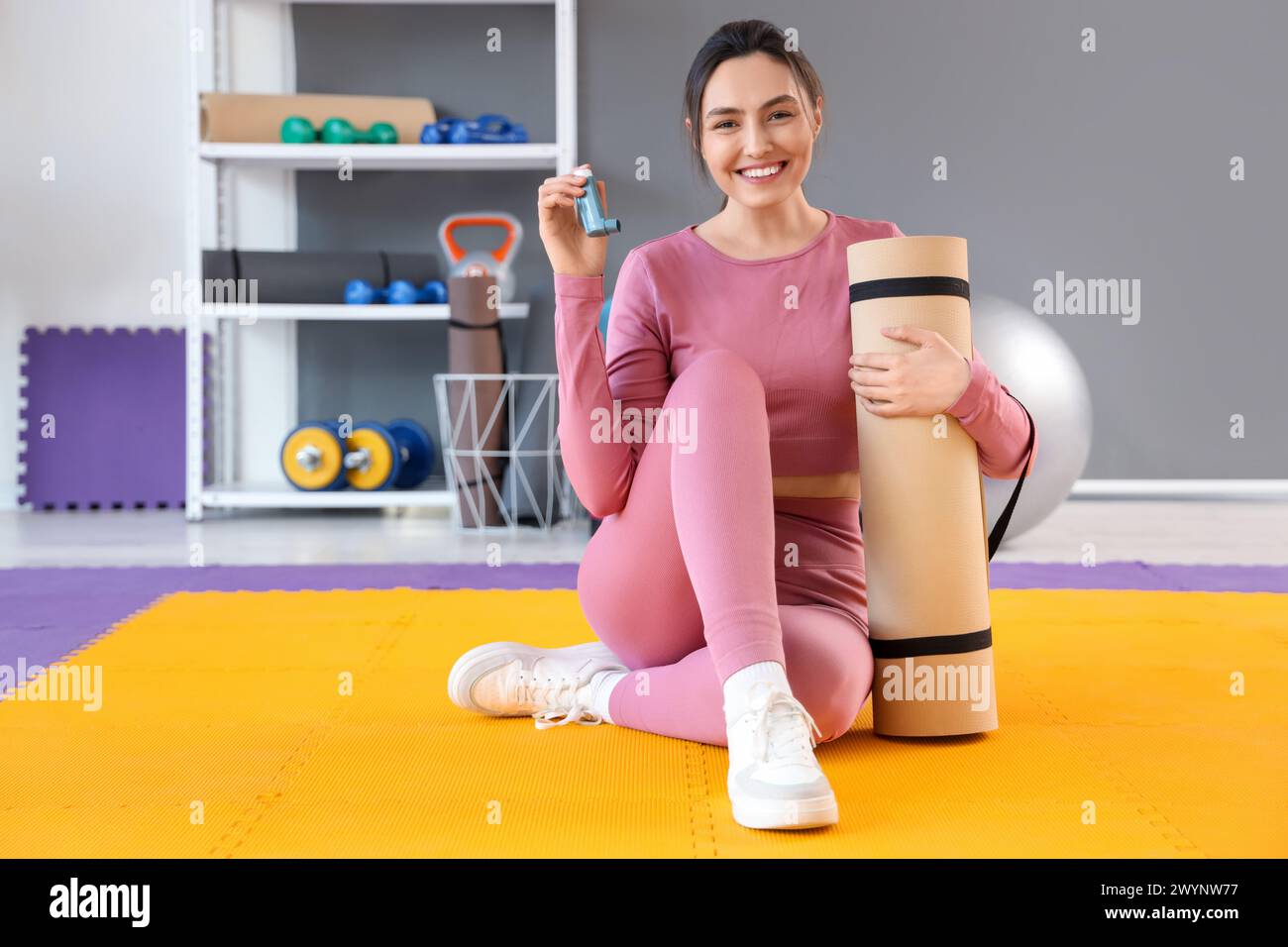 Sporty young woman with inhaler and fitness mat sitting in gym Stock ...