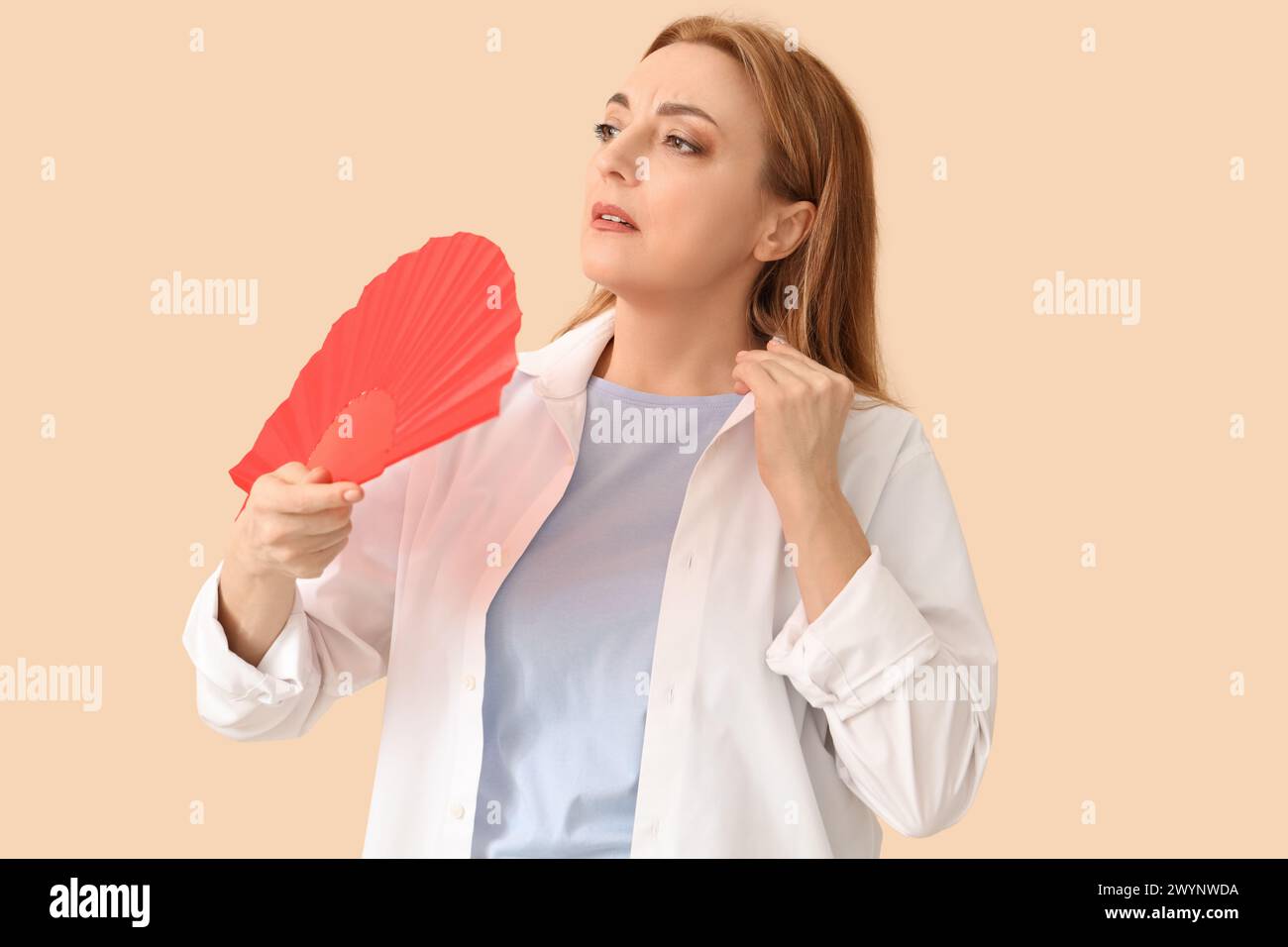 Mature woman with fan suffering from hot flashes on beige background ...