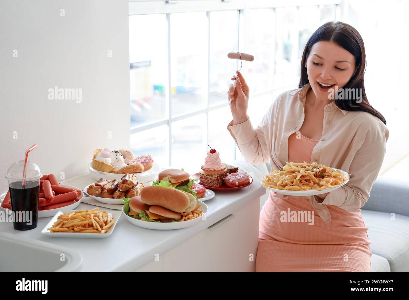 Young woman with unhealthy food on counter in kitchen. Overeating ...