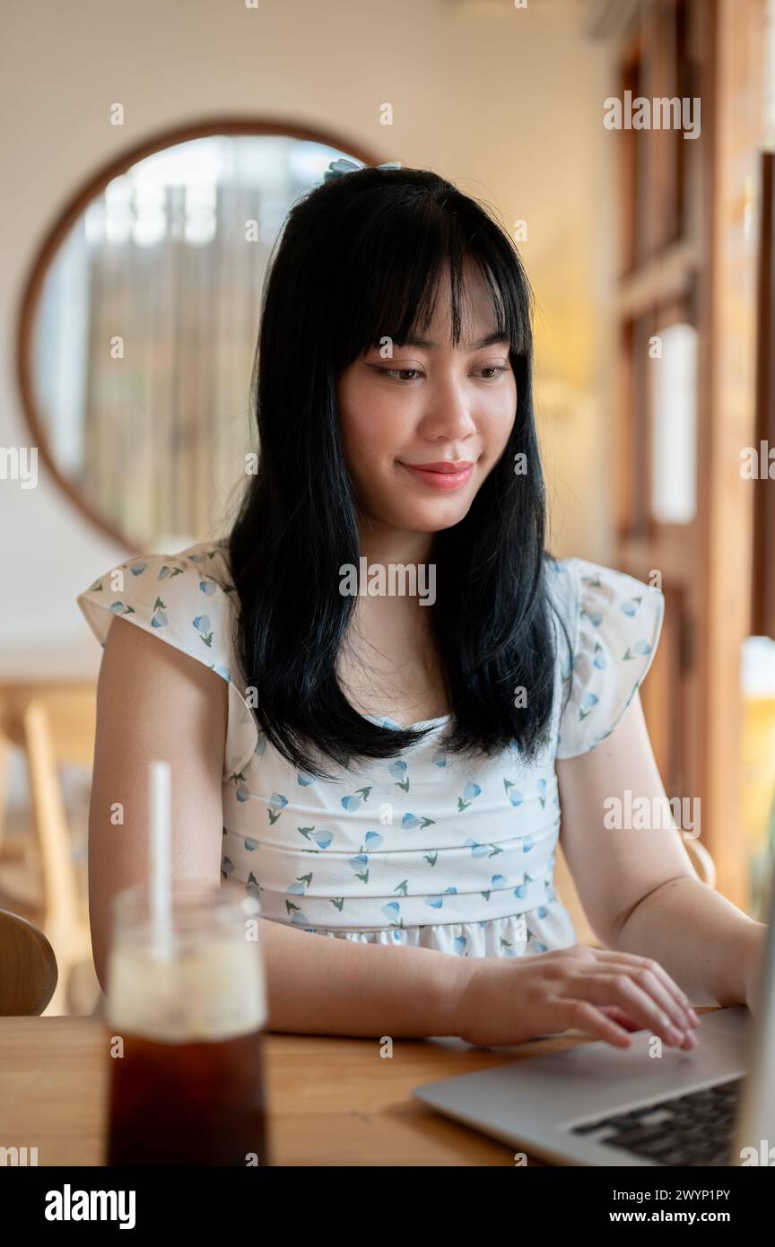 A positive, beautiful young Asian woman in a cute wear is working ...