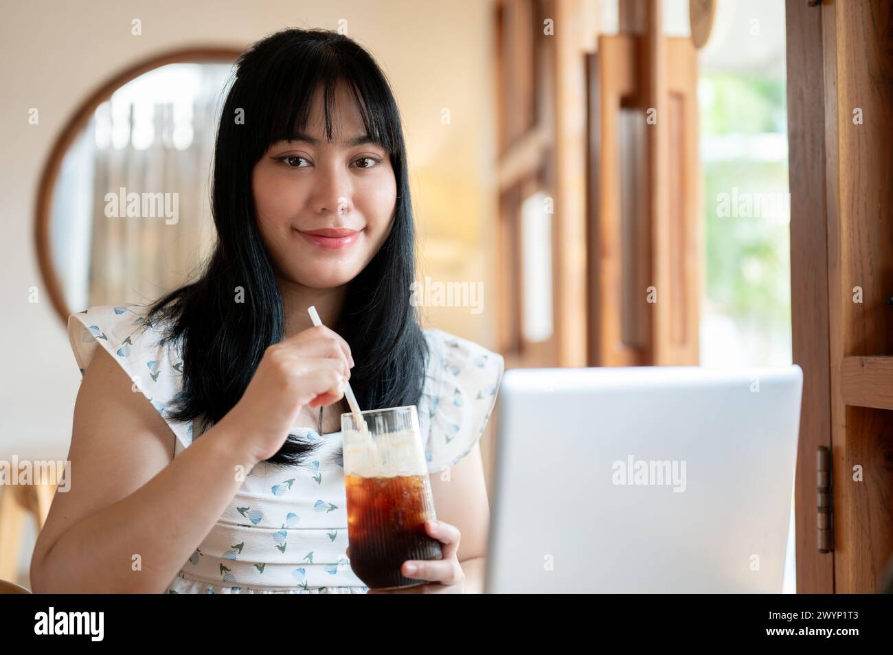 A beautiful, smiling young Asian woman in a cute wear is enjoying iced ...
