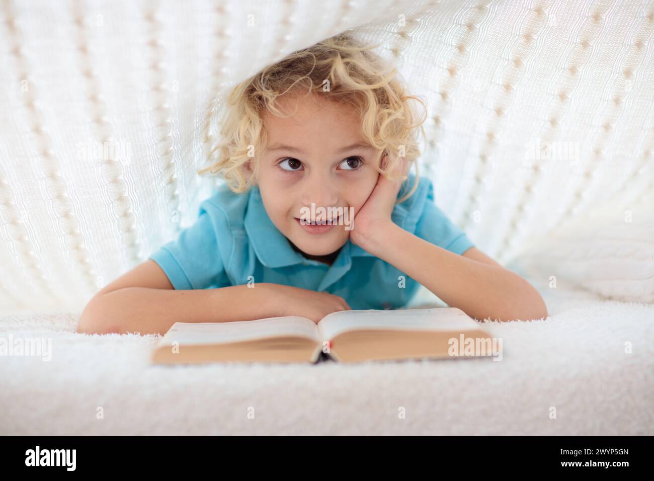Child reading book in bed under knitted blanket. Kids cozy bedroom ...
