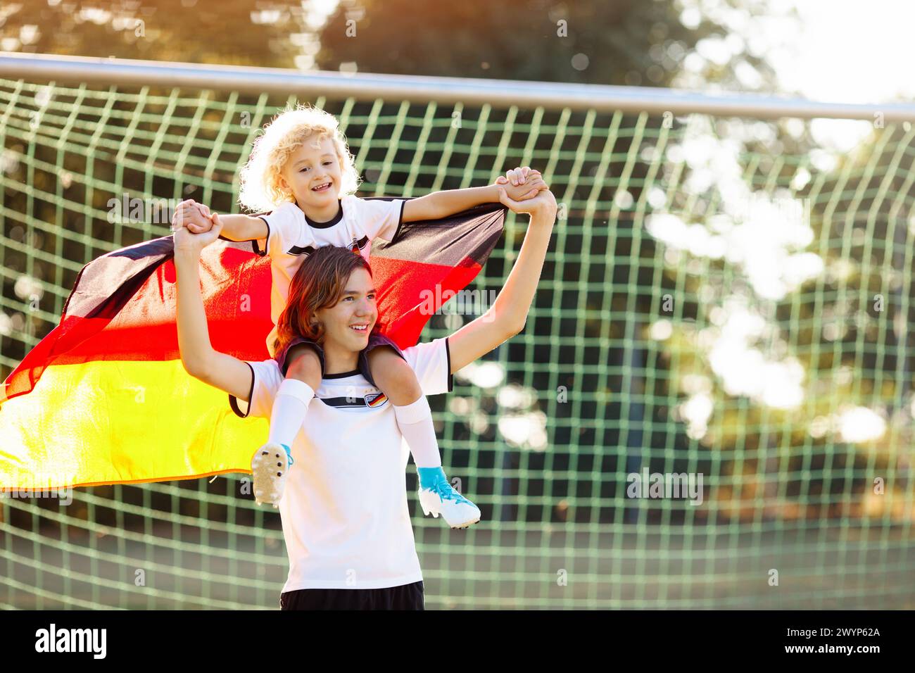 Kids play football on outdoor field. Germany team fans with national flag. Children score a goal ...