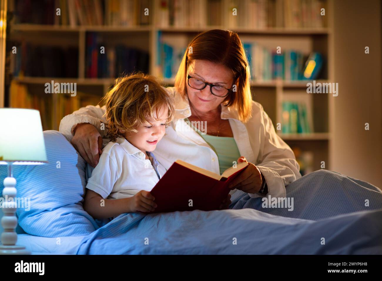 Child reading book in bed. Kids read at night. Little boy and mother with fairy tale books in ...