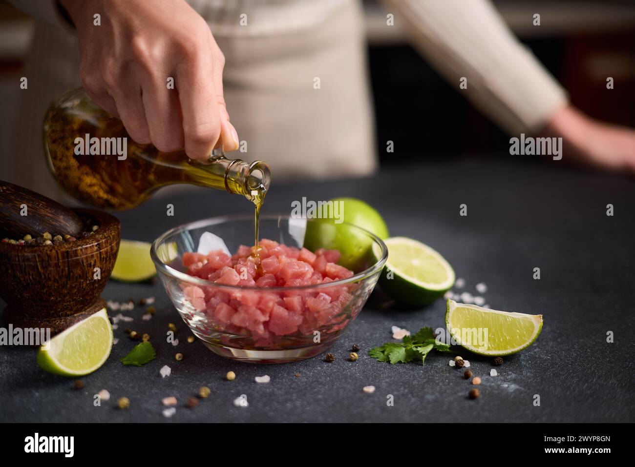 Woman pours cooking olive oil onto Sliced and chopped tuna fillet in ...