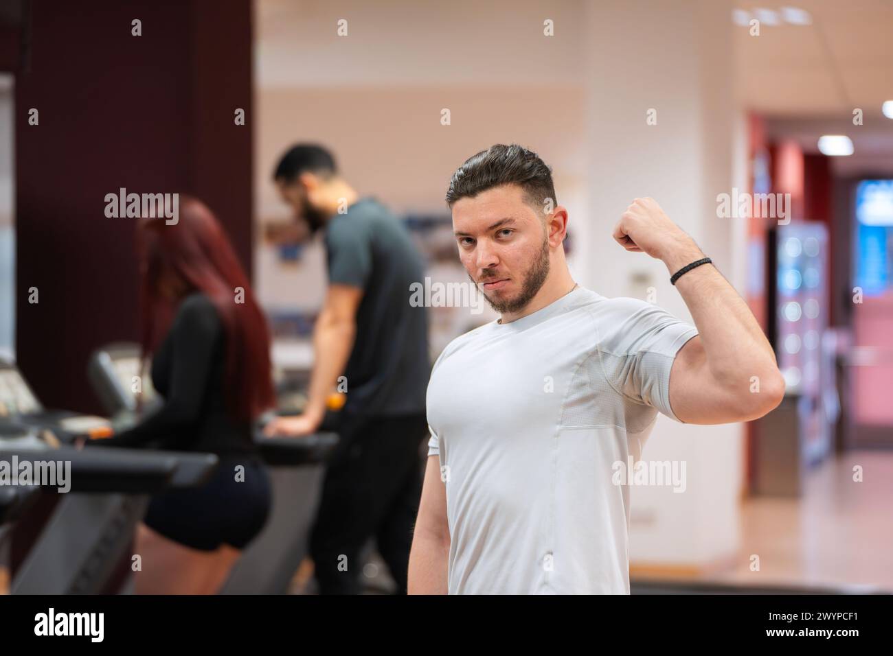 Muscular man in white tee flexes his bicep, with focused gym-goers ...
