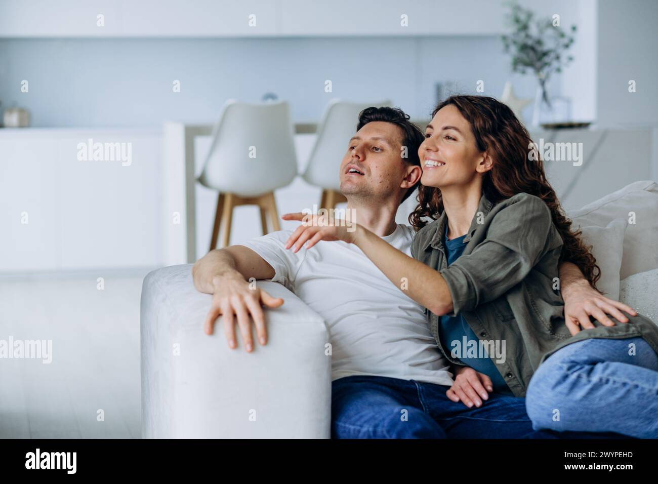 A relaxed couple lounges on a couch in a light-filled living room ...