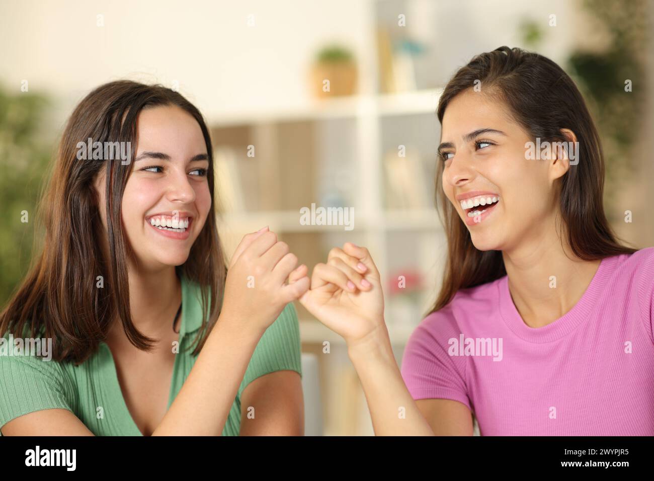 Two happy friends making pinky promise and laughing at home Stock Photo ...