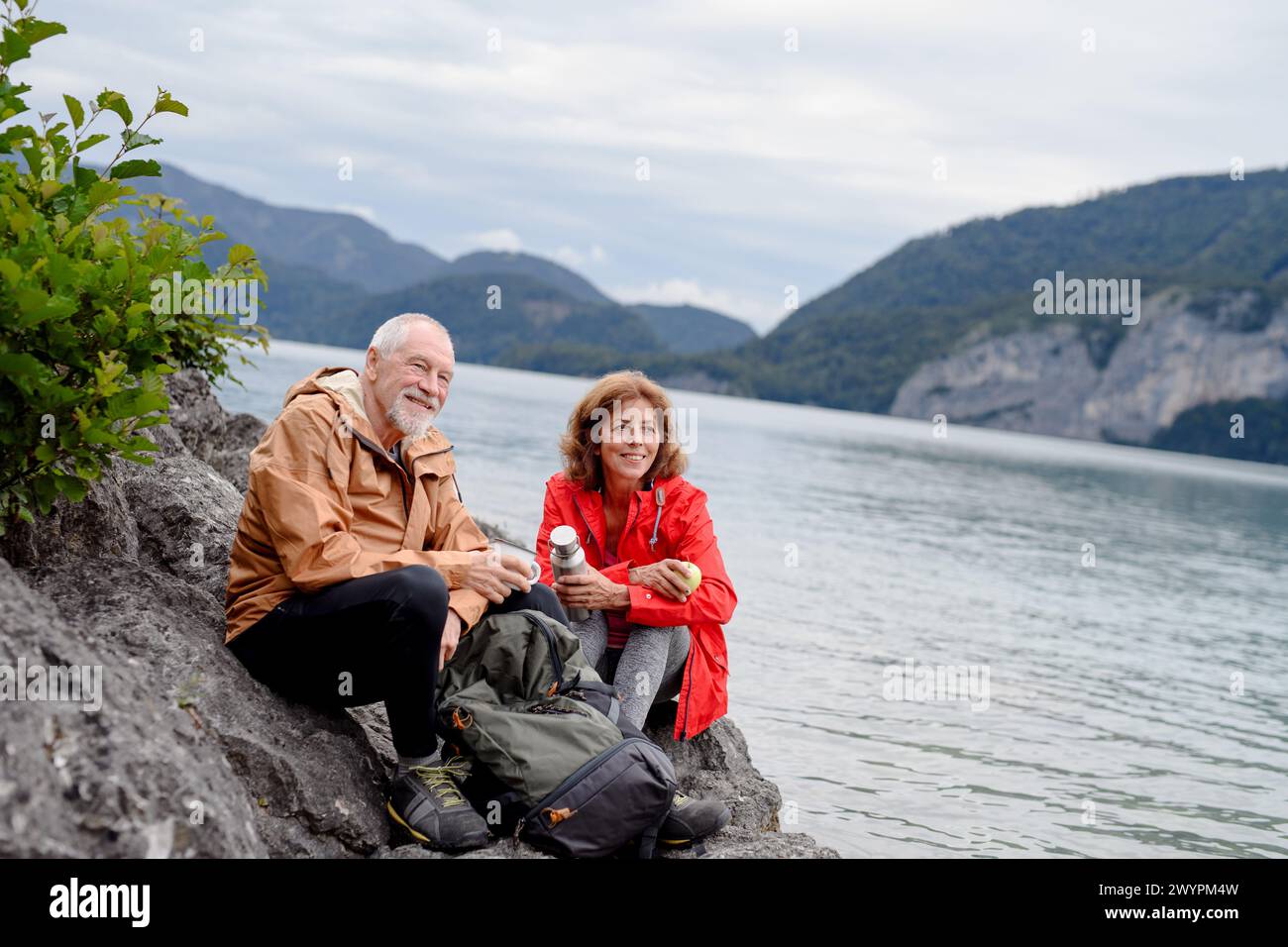 Active elderly couple hiking together in mountains. Drinking coffee and having healthy snack, to ...