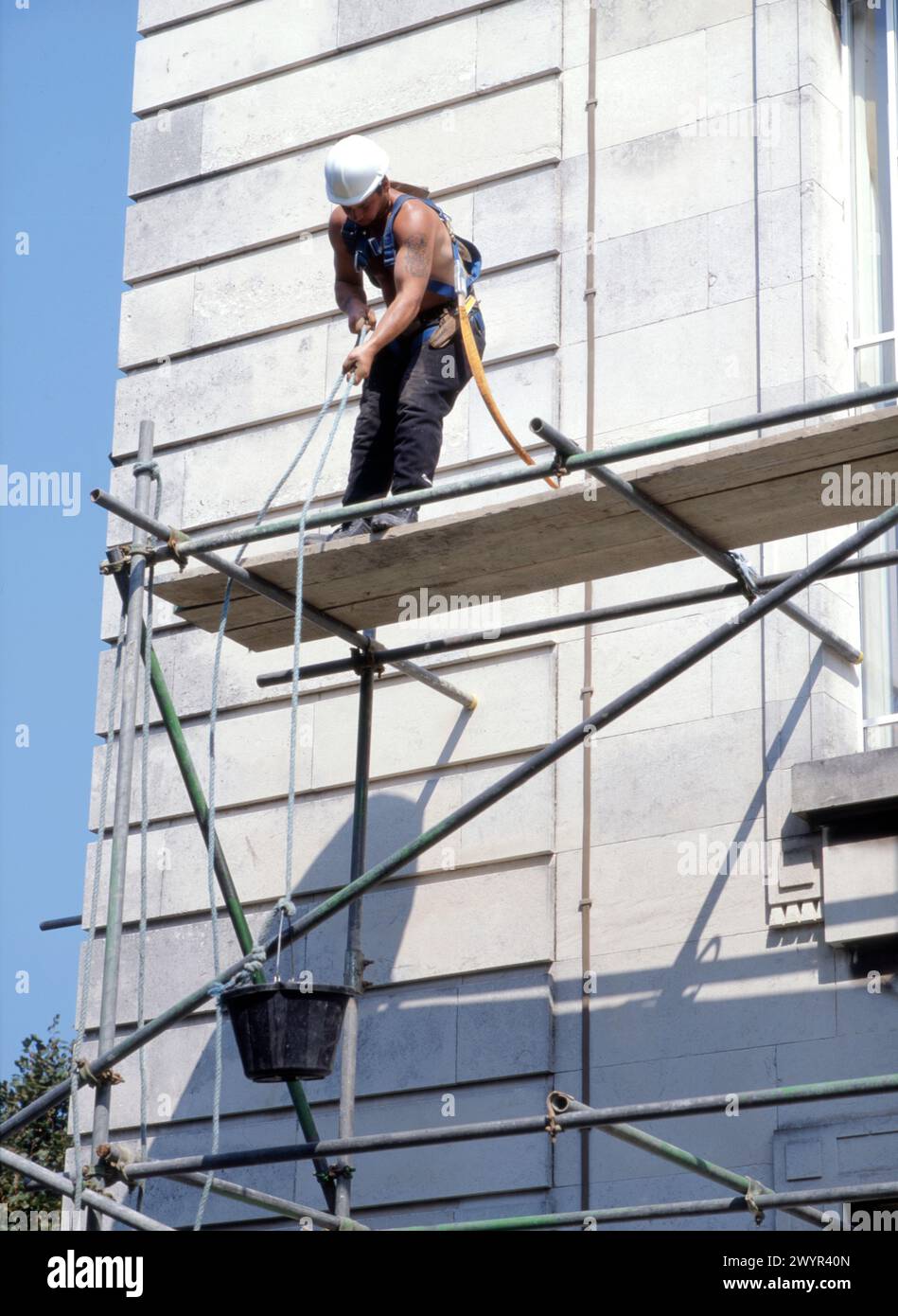 Scaffolder erecting scaffolding outside stone clad building for ...