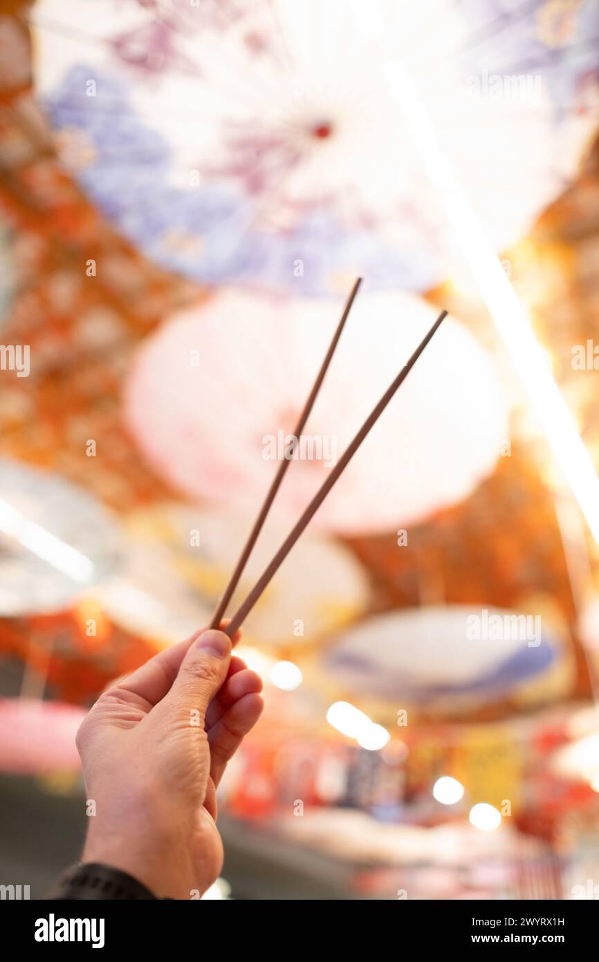 A hand holds two chopsticks for eating Asian food against a warm and ...
