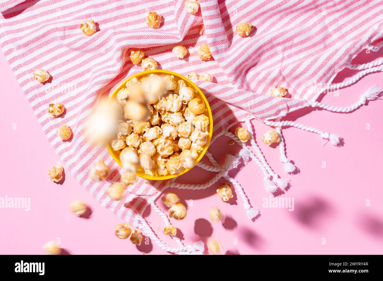Caramelised popcorn dropping down into a yellow bowl, top-side view ...