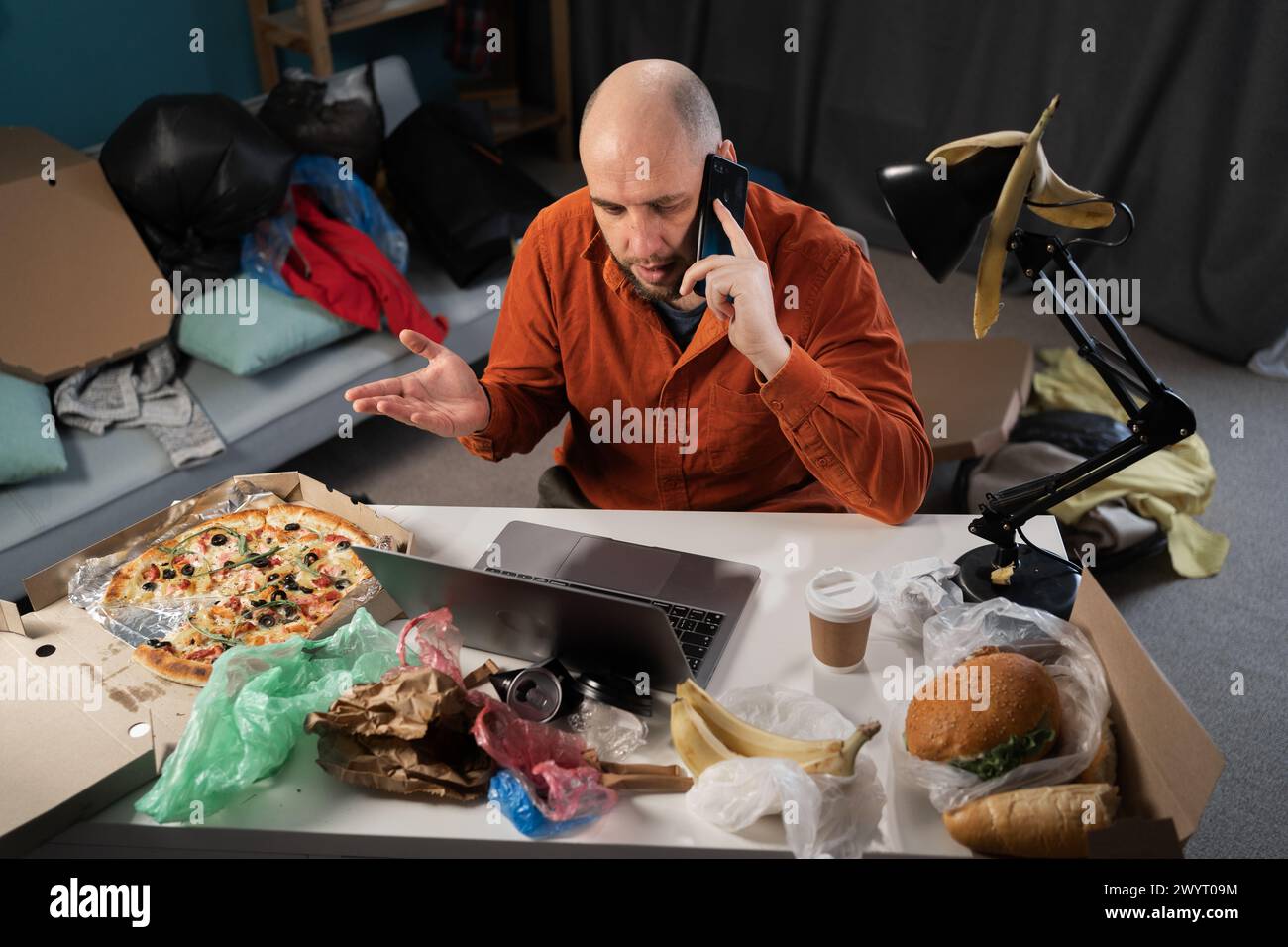 Slatternly bearded man sitting before laptop and holding smartphone ...