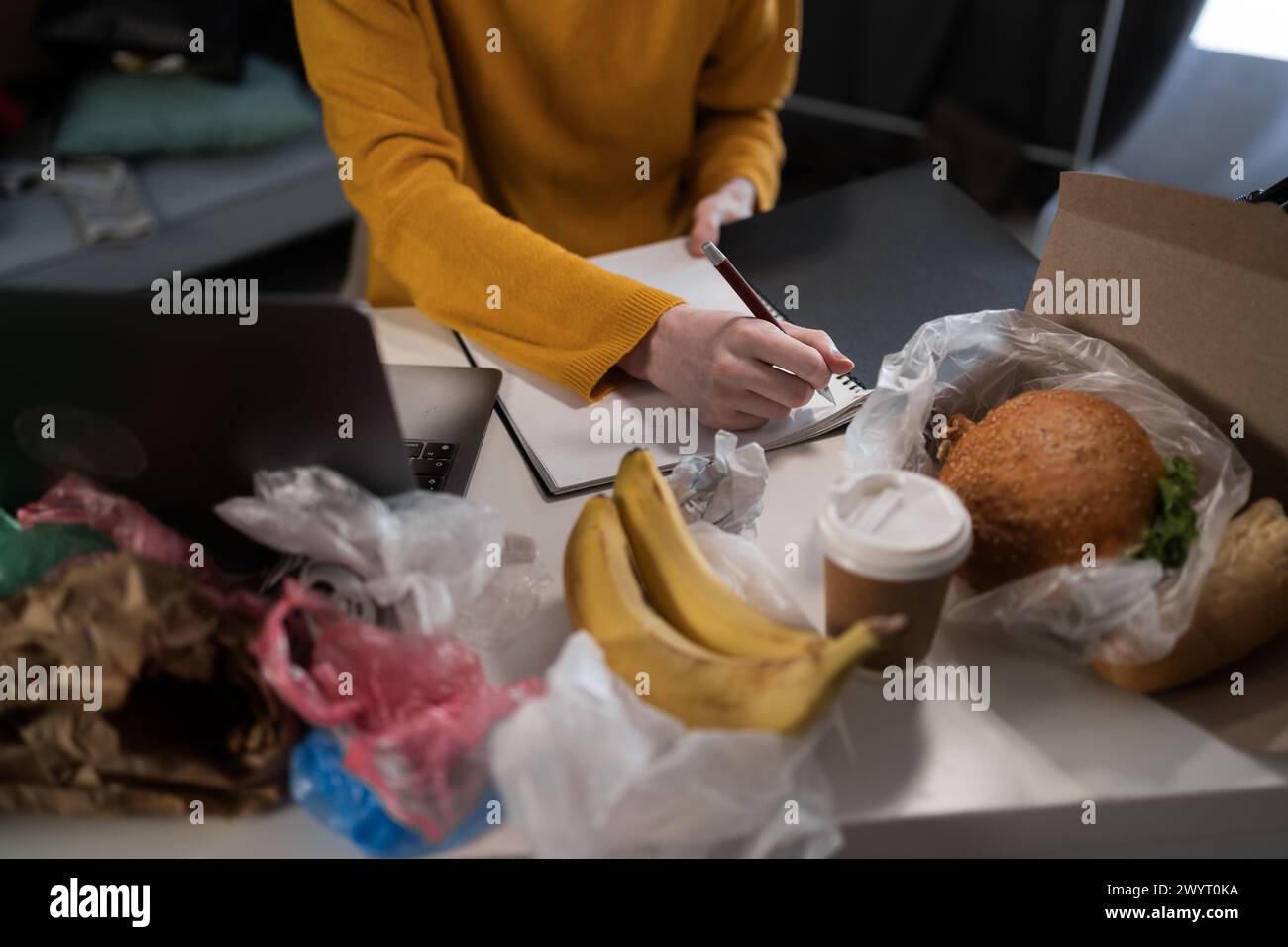 Young man studying in messy room, writing notes on dirty table with ...