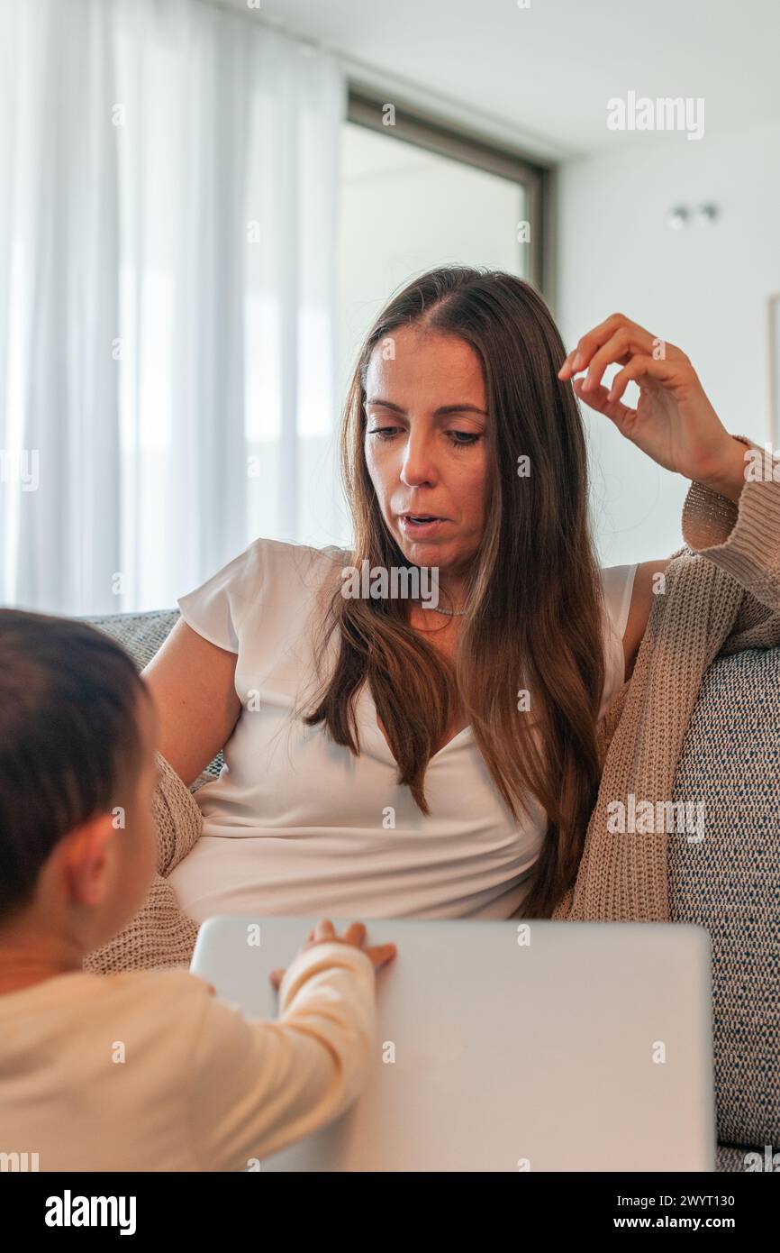 Son Interrupts His Mother Who Is Sitting On The Sofa Working On Her