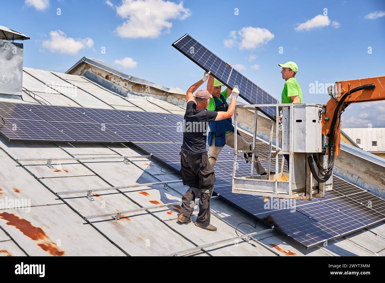 Workers lifting up photovoltaic solar panel on metal rooftop of house ...