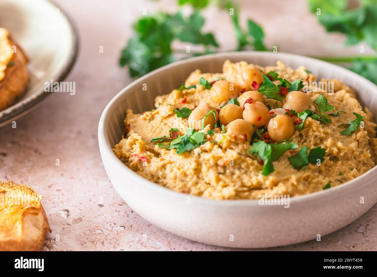Hummus, chickpea puree with coriander in a bowl on light background ...