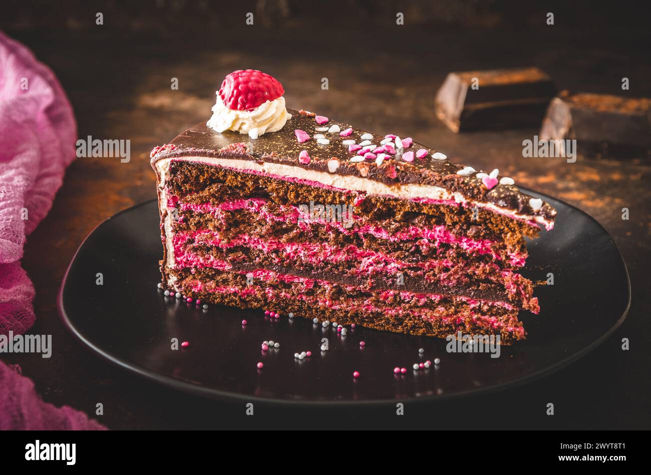 Piece of raspberry chocolate torte on a black plate on dark brown ...