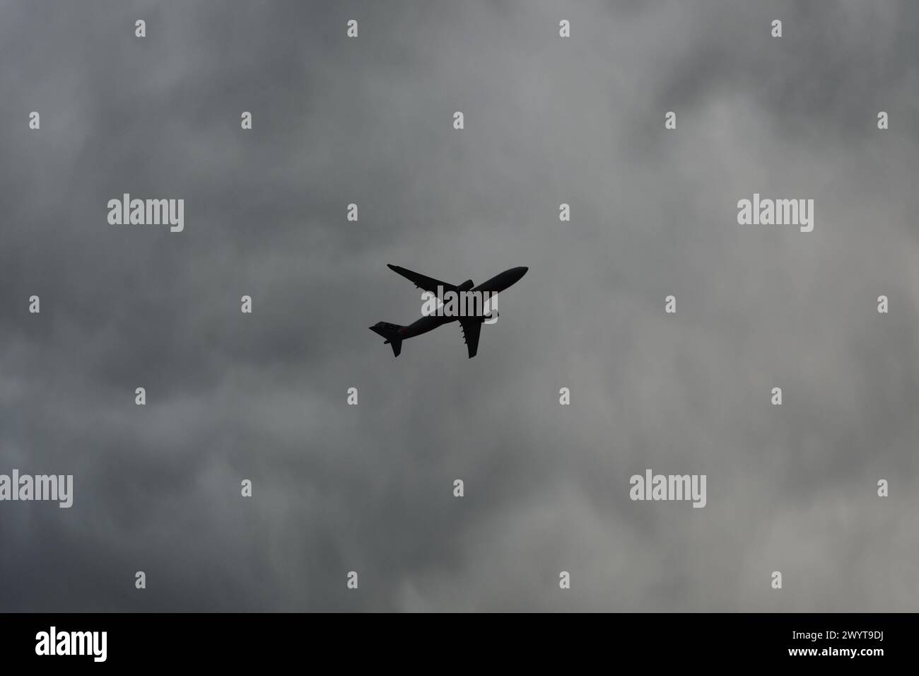 Silhouette of a commercial jet airliner against a mass of low grey ...