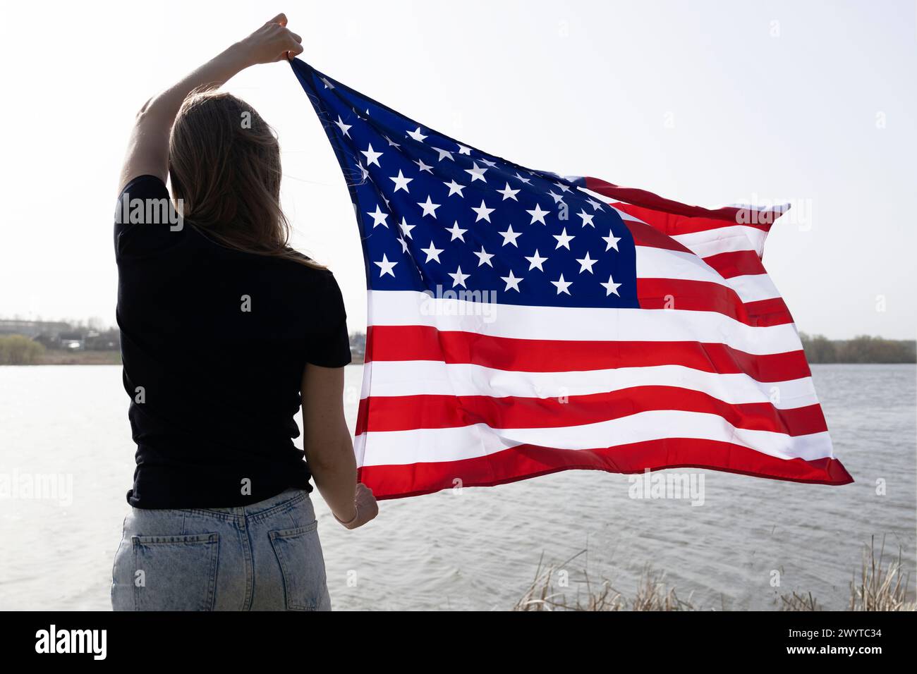 woman stands with her back and holds a large American flag at her side ...