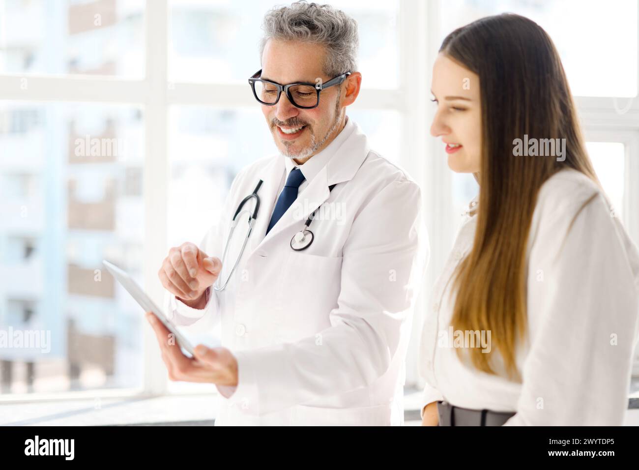 A distinguished doctor with silver hair consults a tablet alongside a ...