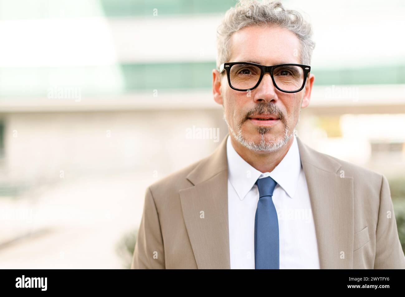 A senior businessman in glasses with grey hair poses confidently ...