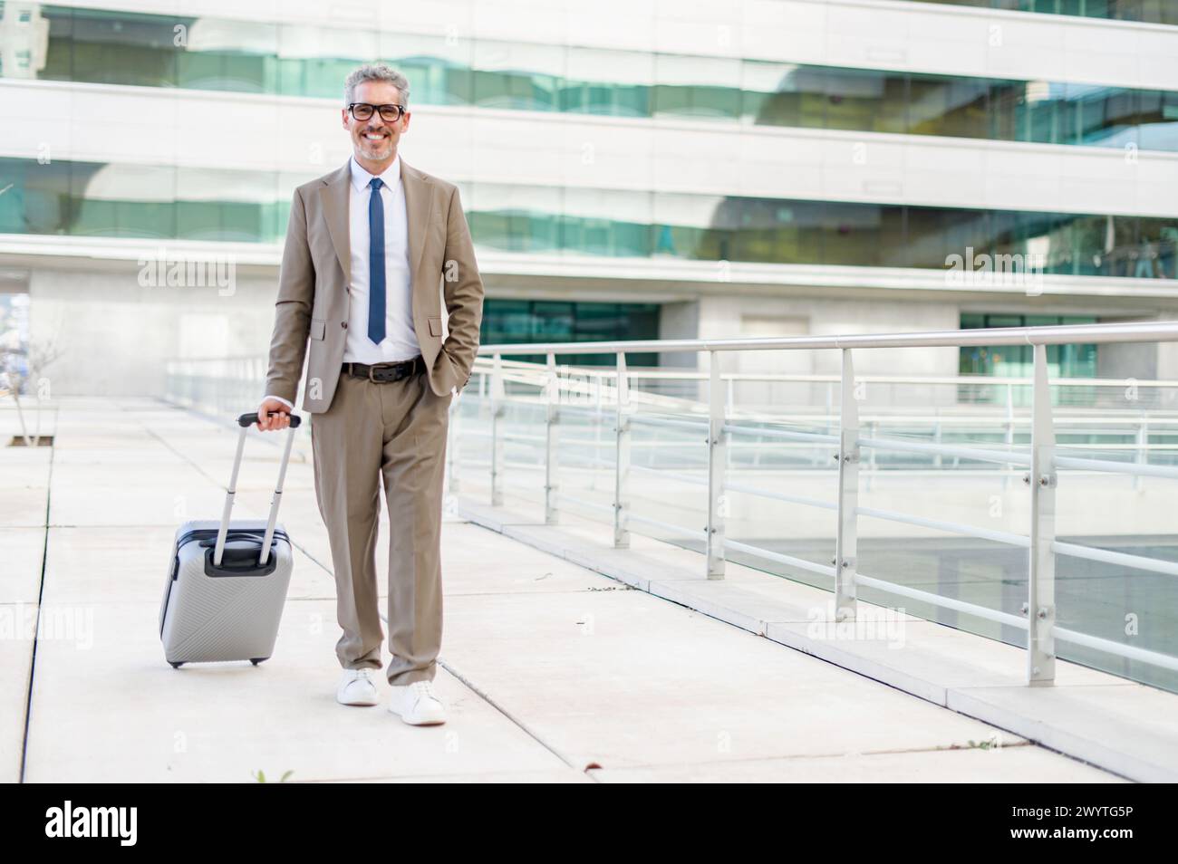 A charismatic businessman with a suitcase poses confidently outdoors ...