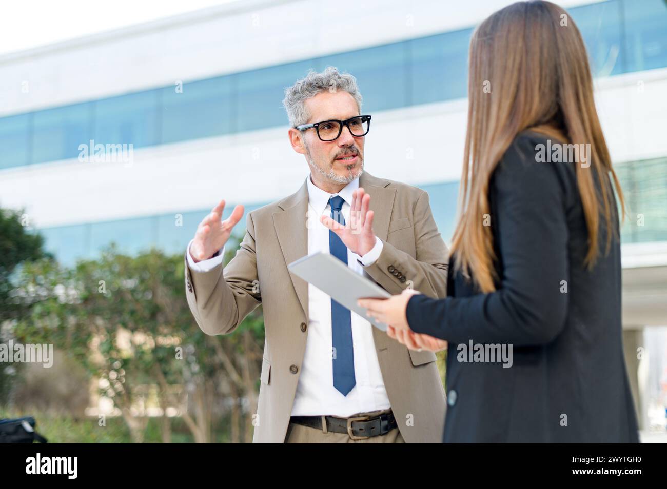 In a casual outdoor meeting, a grey-haired businessman animatedly ...