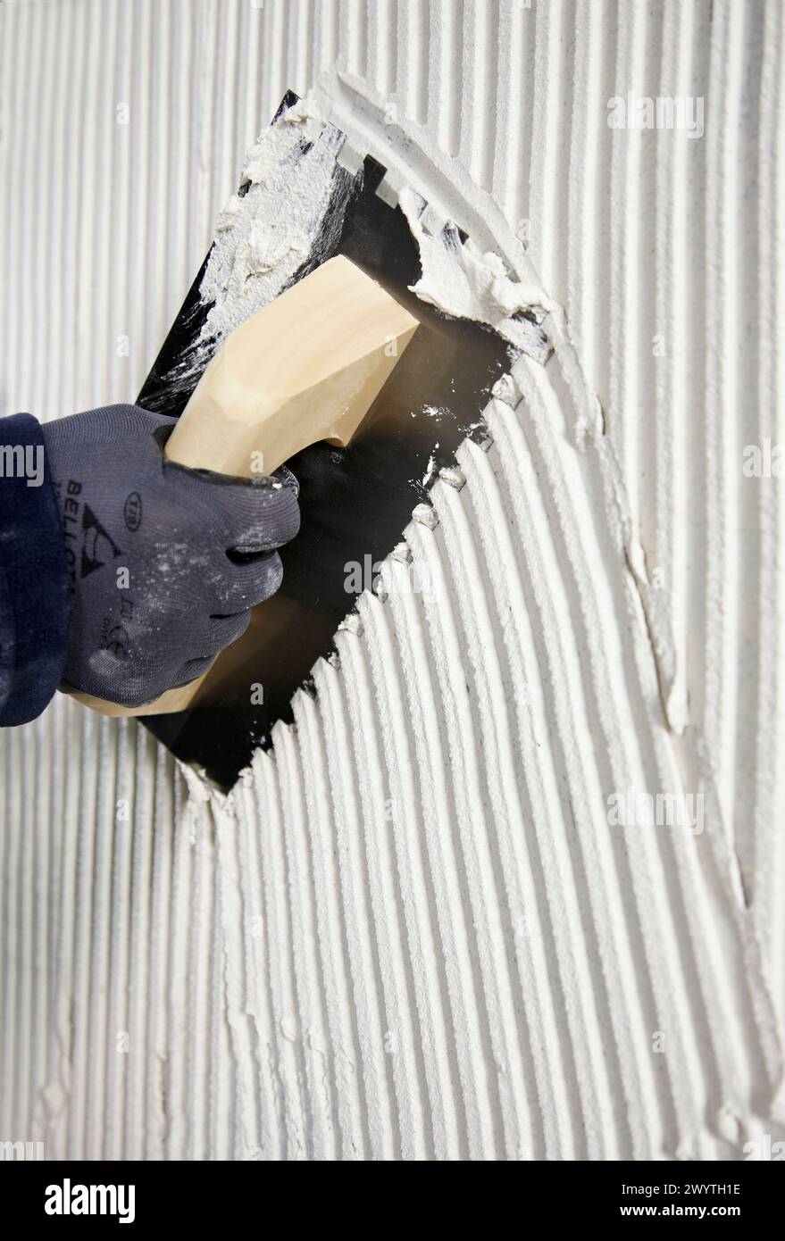 Preparing wall with glue mortar before tiling using a serrated ...