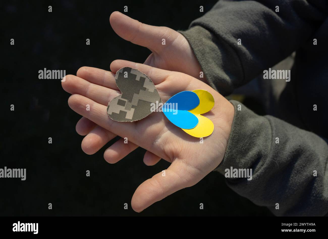 heart cut out of military camouflage fabric and yellow blue paper lies ...