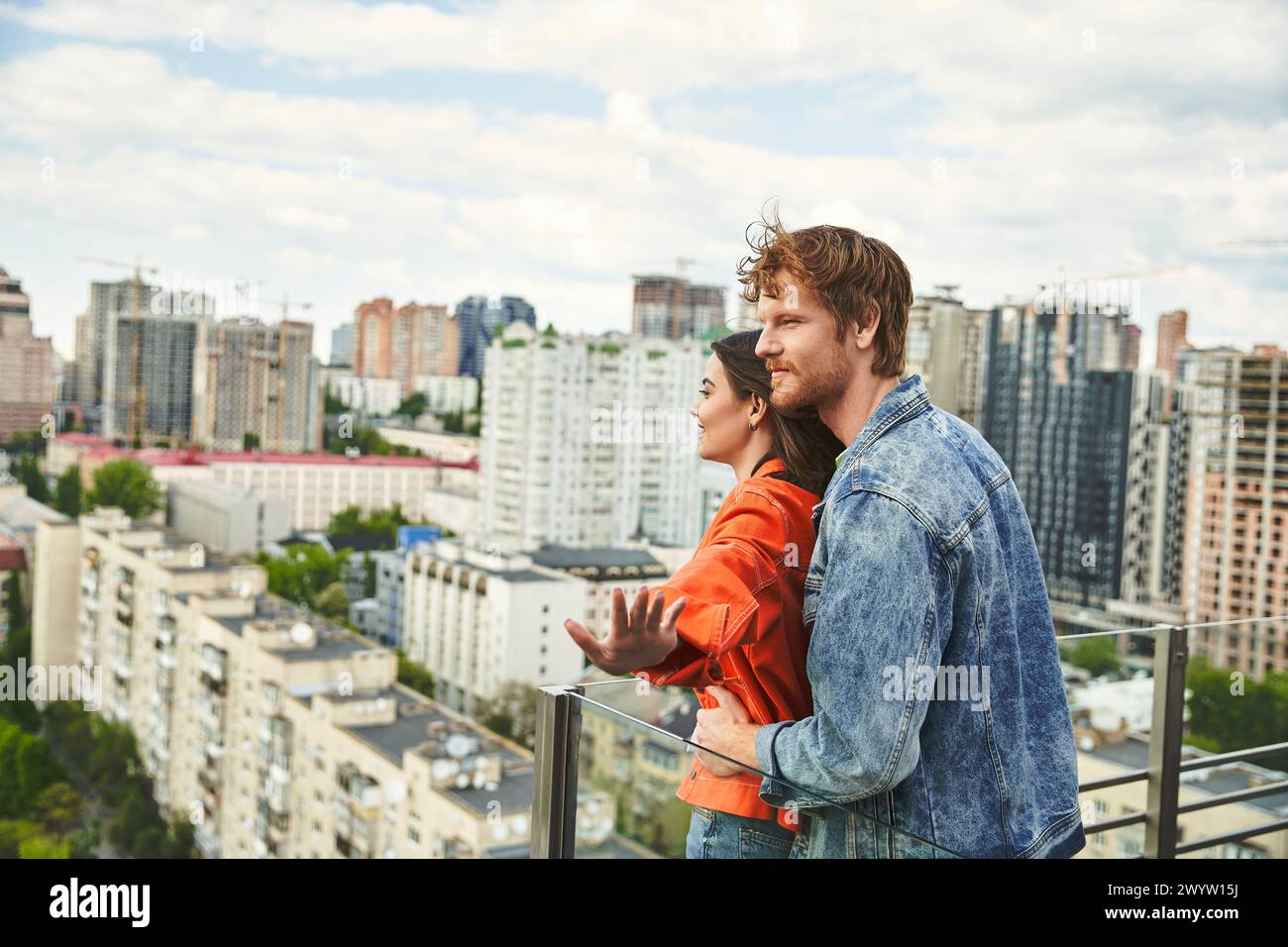 A man and woman stand on a balcony, gazing at a sprawling city below ...