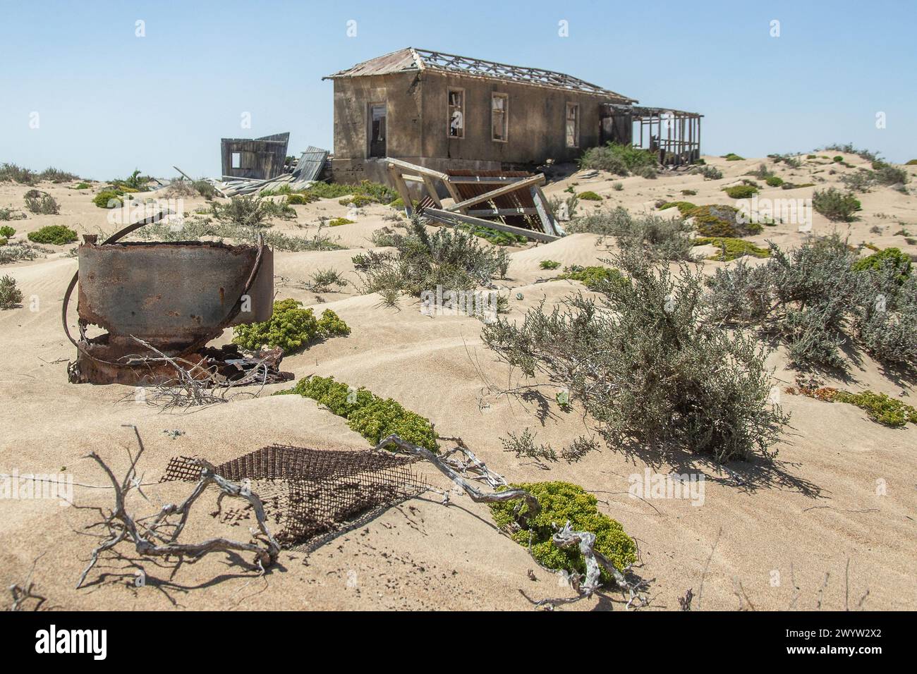 Rusting items lying in the sand by an abandoned, miner's house ...