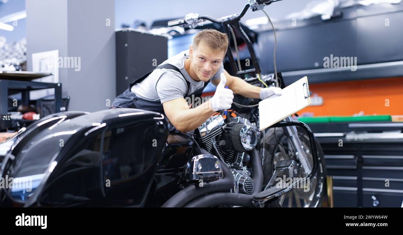 Young car mechanic is diagnosing a motorcycle and holding clipboard and ...