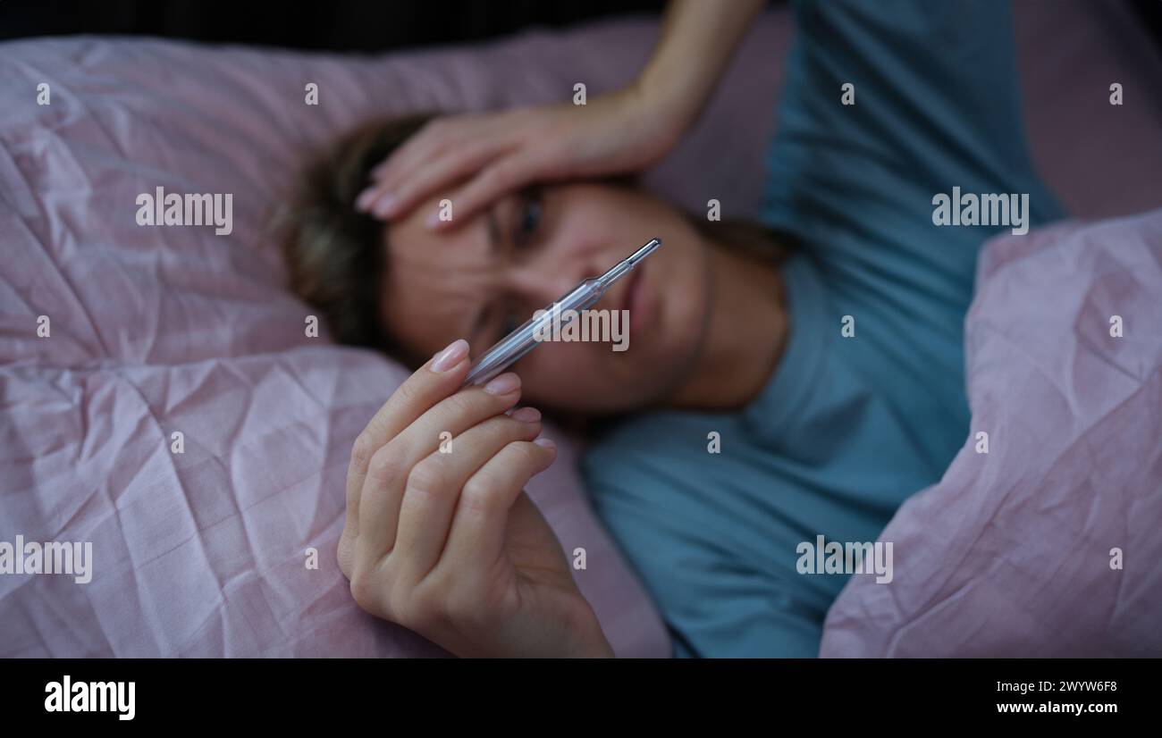 Sick woman lying in bed and holding thermometer with high temperature ...