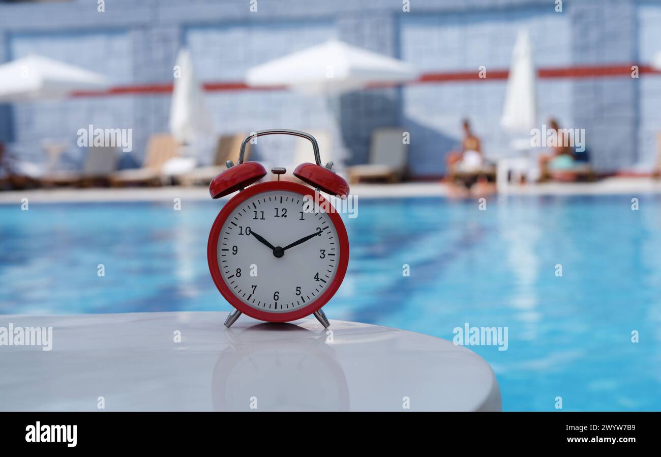 Red analog alarm clock with blurred background of relaxation pool Stock ...