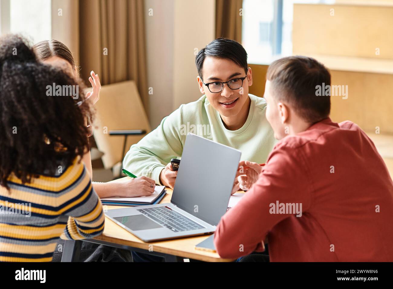 Diverse group of students sitting around a table with laptops, working together on projects and ...