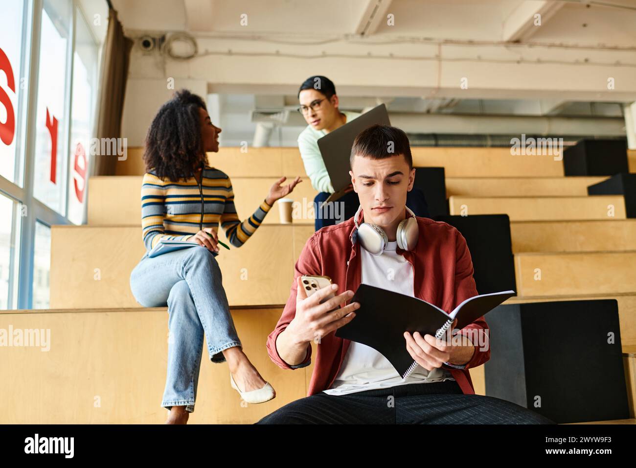 A man engrossed in a book, seated in a lecture hall surrounded by ...
