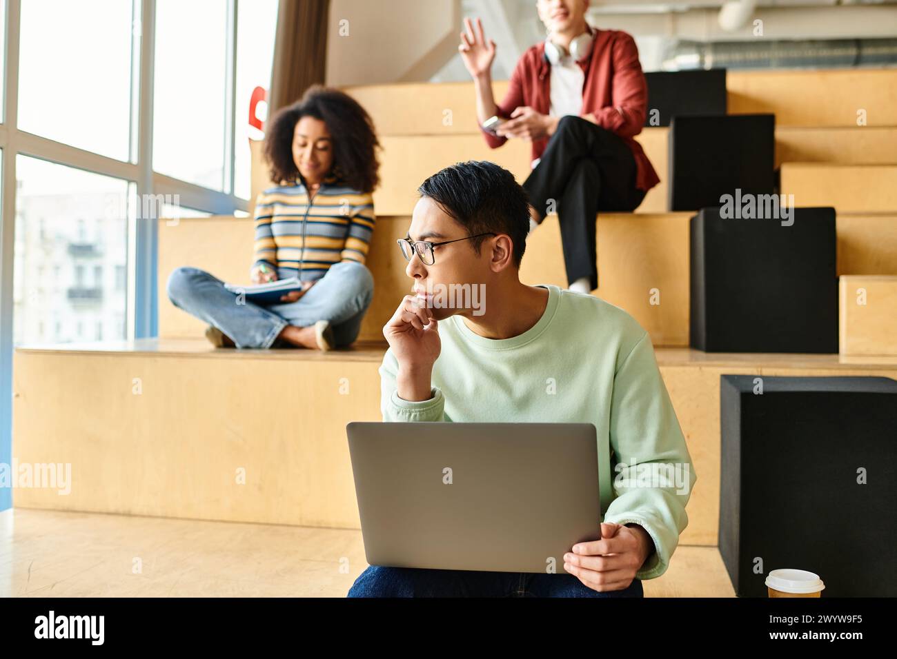 A man, laptop open, sits cross-legged on the floor intently working on ...