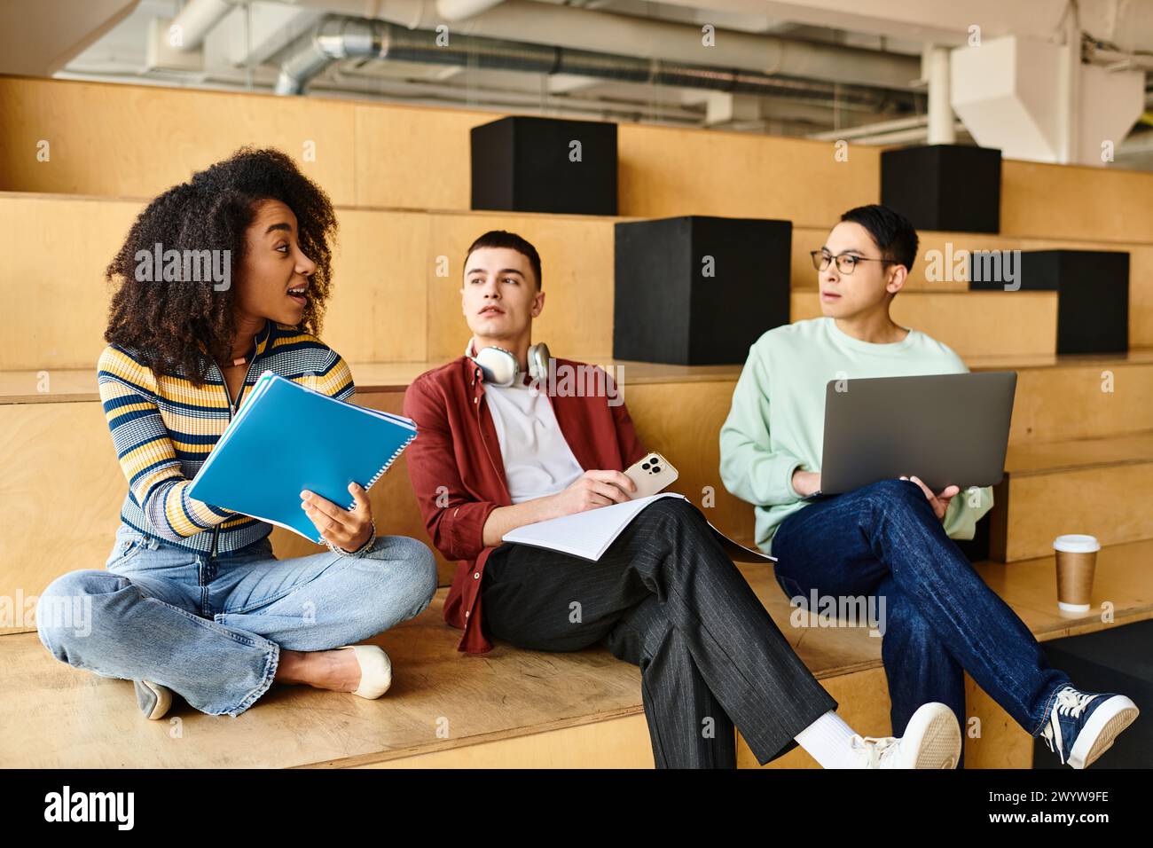 Multicultural students sitting on stage with laptops, participating in ...