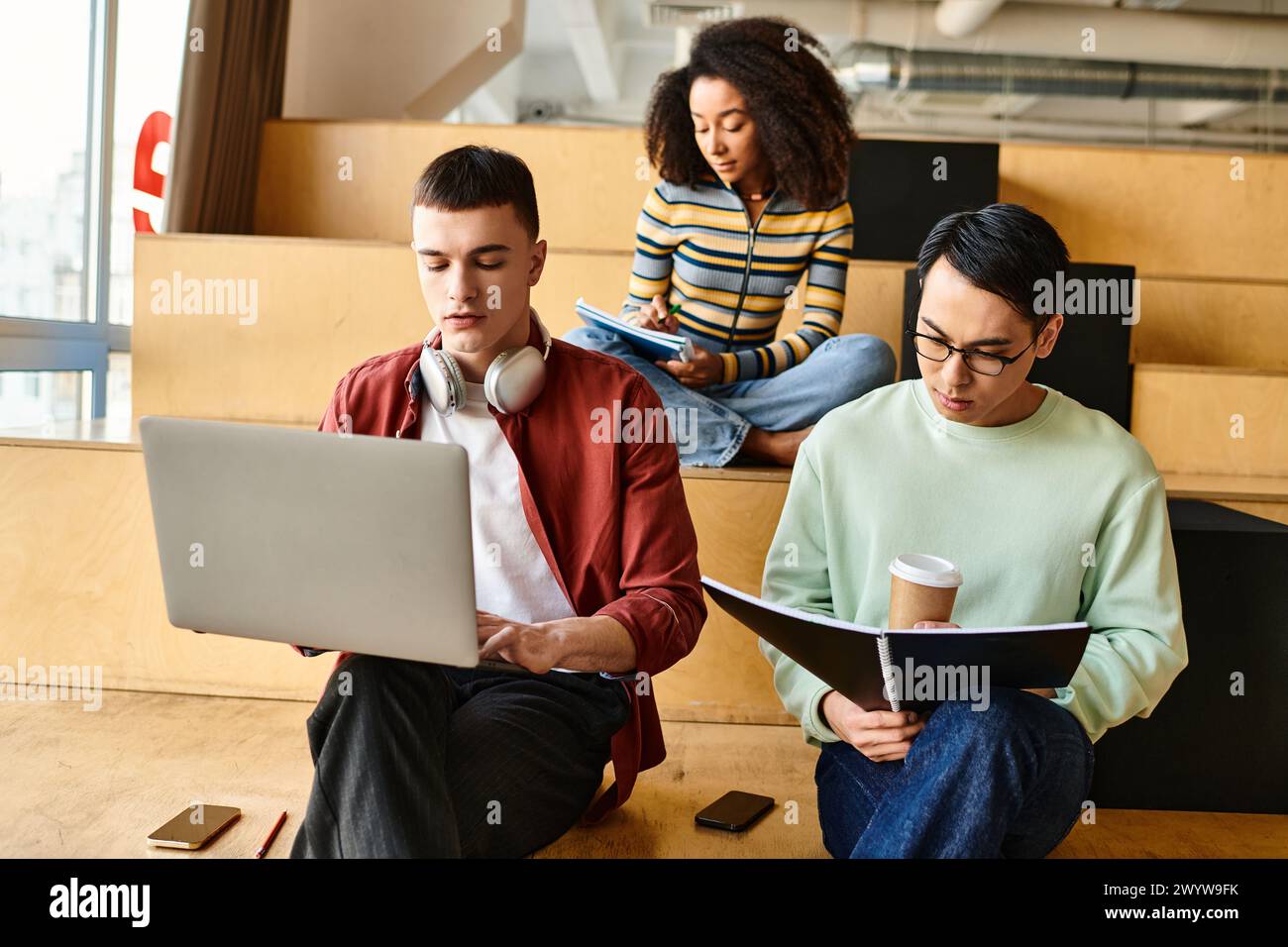 Multicultural students sit on floor with laptops, immersed in digital ...