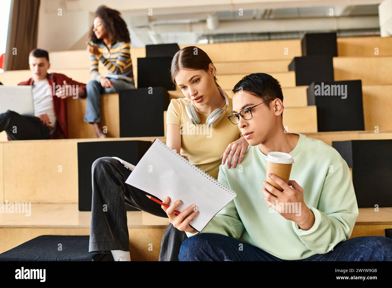 A man and woman, students, sit on a bench, studying a piece of paper ...