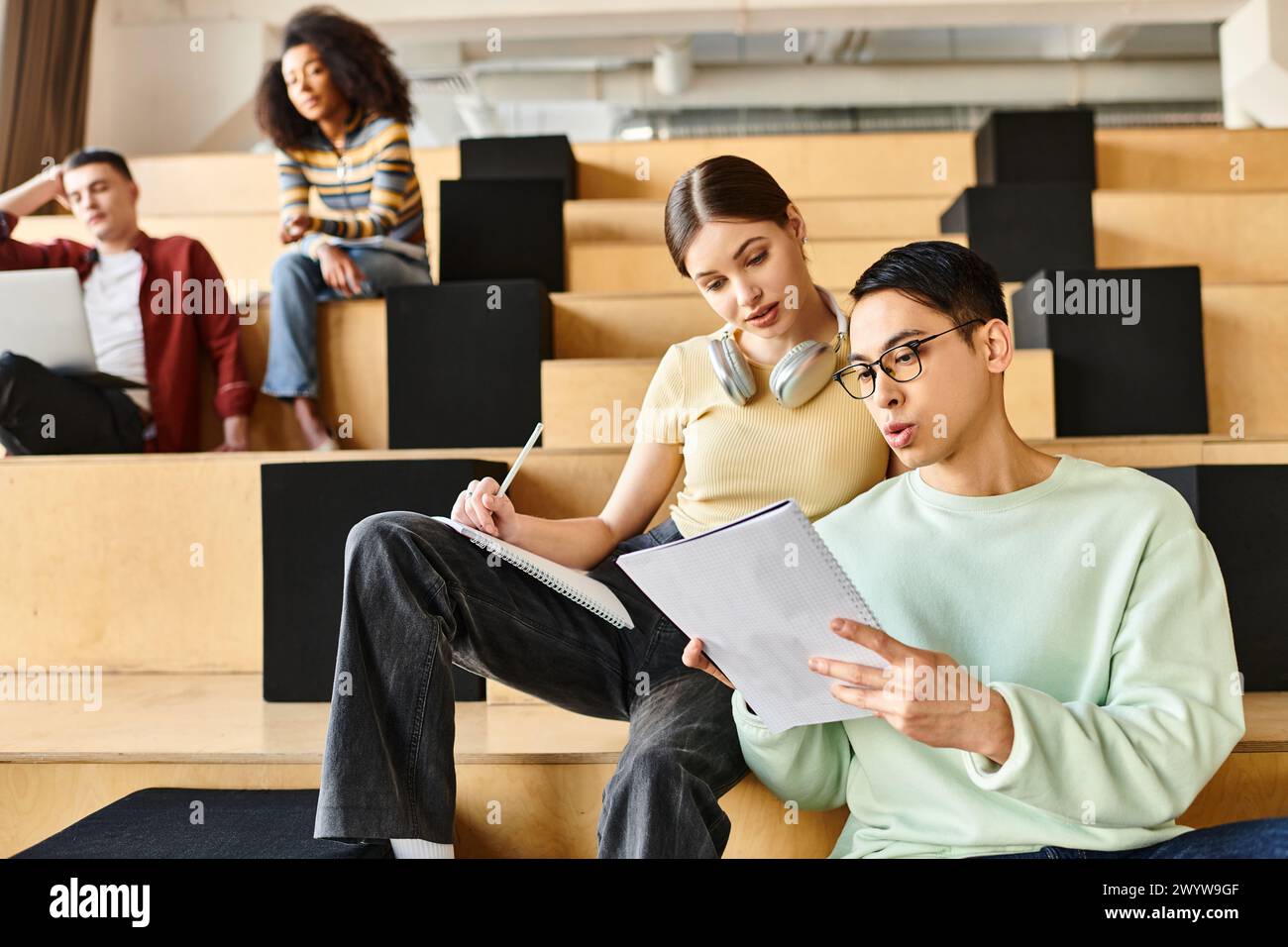 A man and a woman of diverse backgrounds sit on lecture hall steps ...