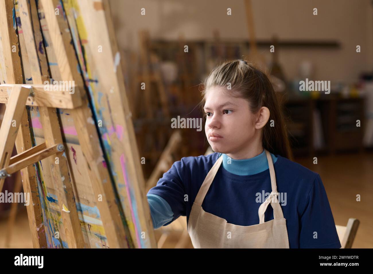 Side view portrait of young girl with disability painting on canvas in ...
